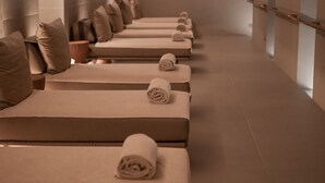Uma sala de spa com várias mesas de massagem dispostas em linha, cada uma com uma toalha enrolada.