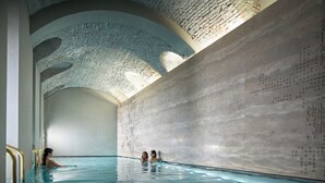 Piscina interior com teto abobadado alto e parede com inscrições.