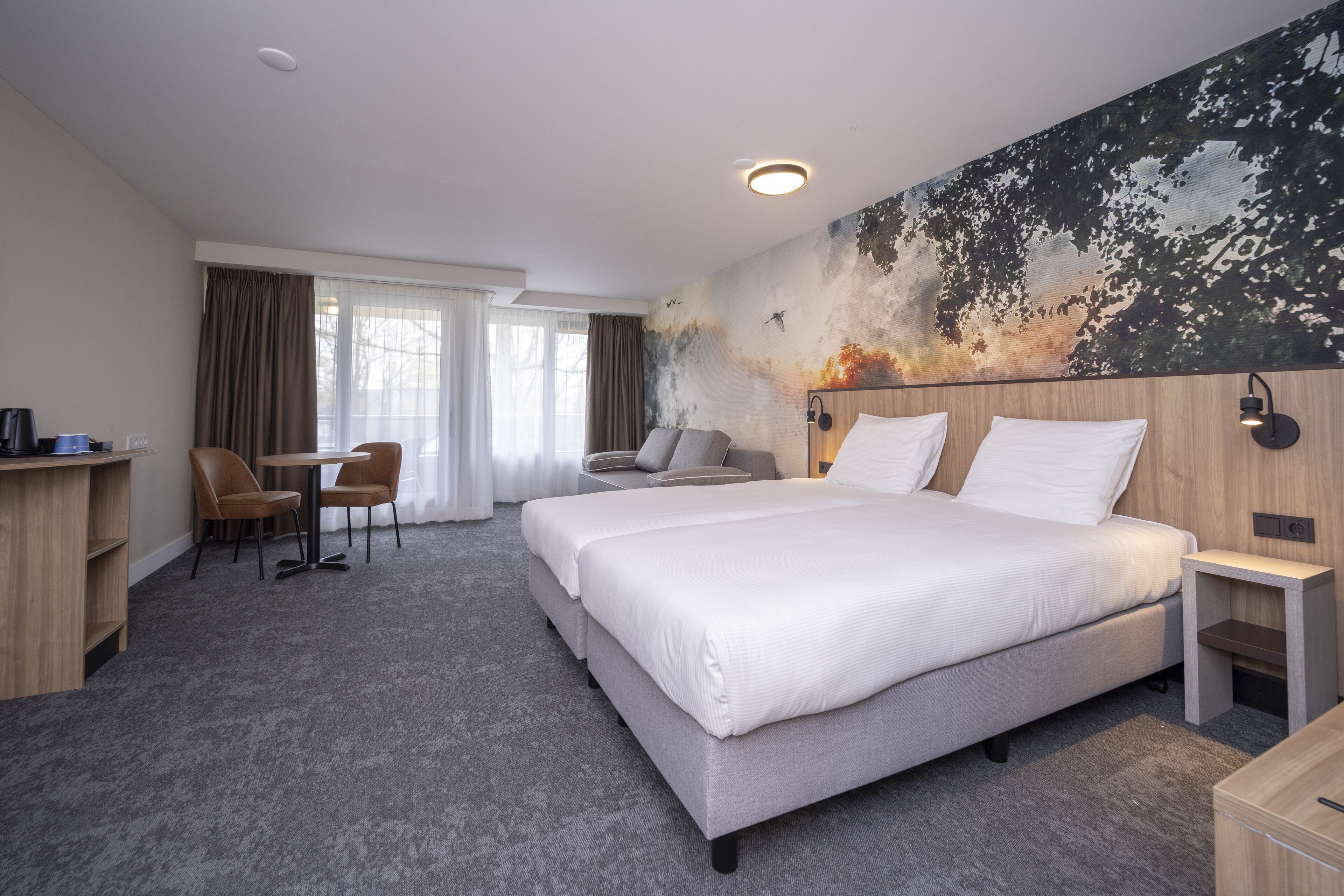 Quarto de hotel com uma cama grande, uma escrivaninha, uma cadeira e televisão fixada na parede.
