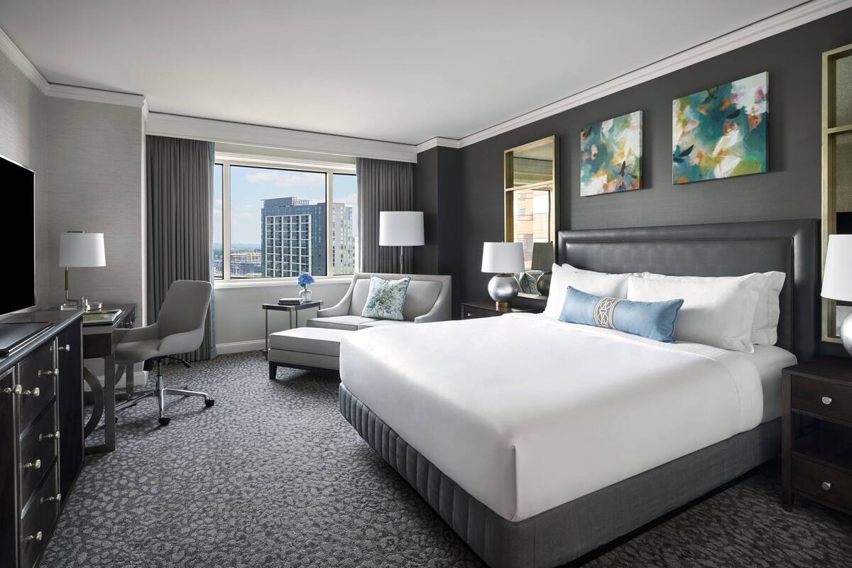 Quarto de hotel moderno com uma cama grande, uma escrivaninha, uma cadeira e uma televisão.