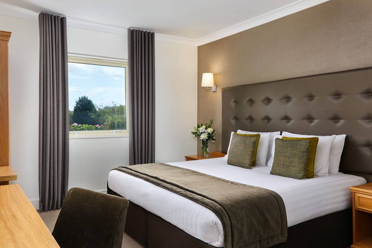 Quarto de hotel com uma cama grande, uma escrivaninha de madeira e uma janela com cortinas.