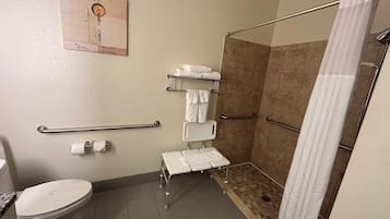 Uma casa de banho com acessibilidade para cadeira de rodas, com chuveiro, sanita e barras de apoio.