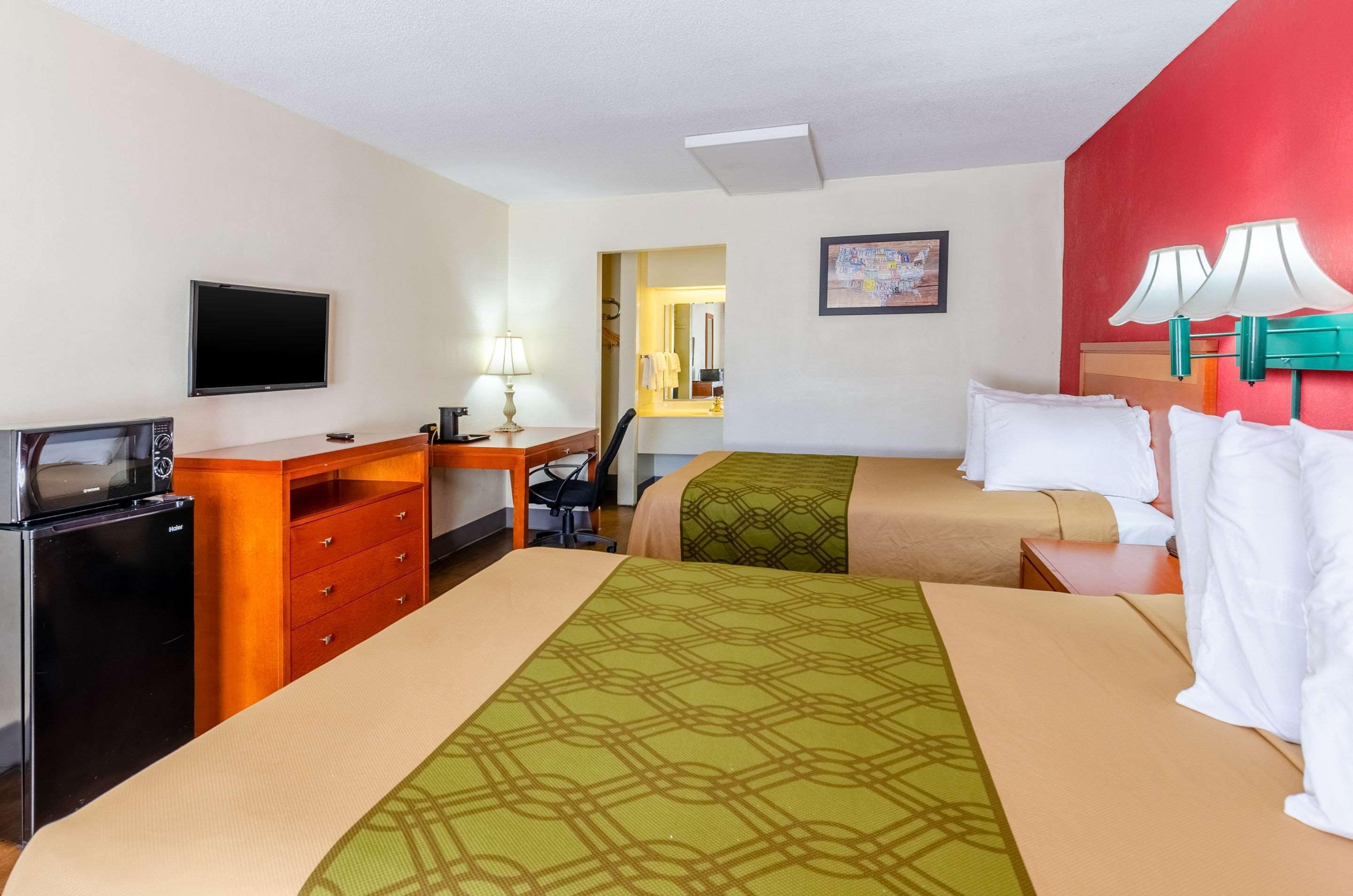 Quarto de hotel com duas camas, uma escrivaninha com abajur, televisão e frigorífico.