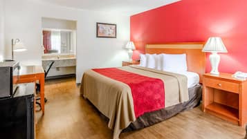 Quarto de hotel com cama, mesas de cabeceira, escrivaninha, cadeira, espelho e parede com detalhe em vermelho.
