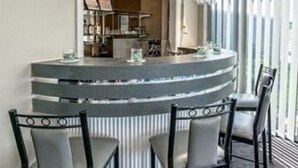 Uma área de bar com balcão curvo, banquetas e vista para a cozinha ao fundo.