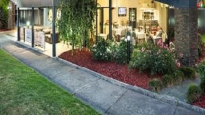 Um hotel com um jardim bem cuidado, um caminho pavimentado e uma área de jantar visível pelas janelas.