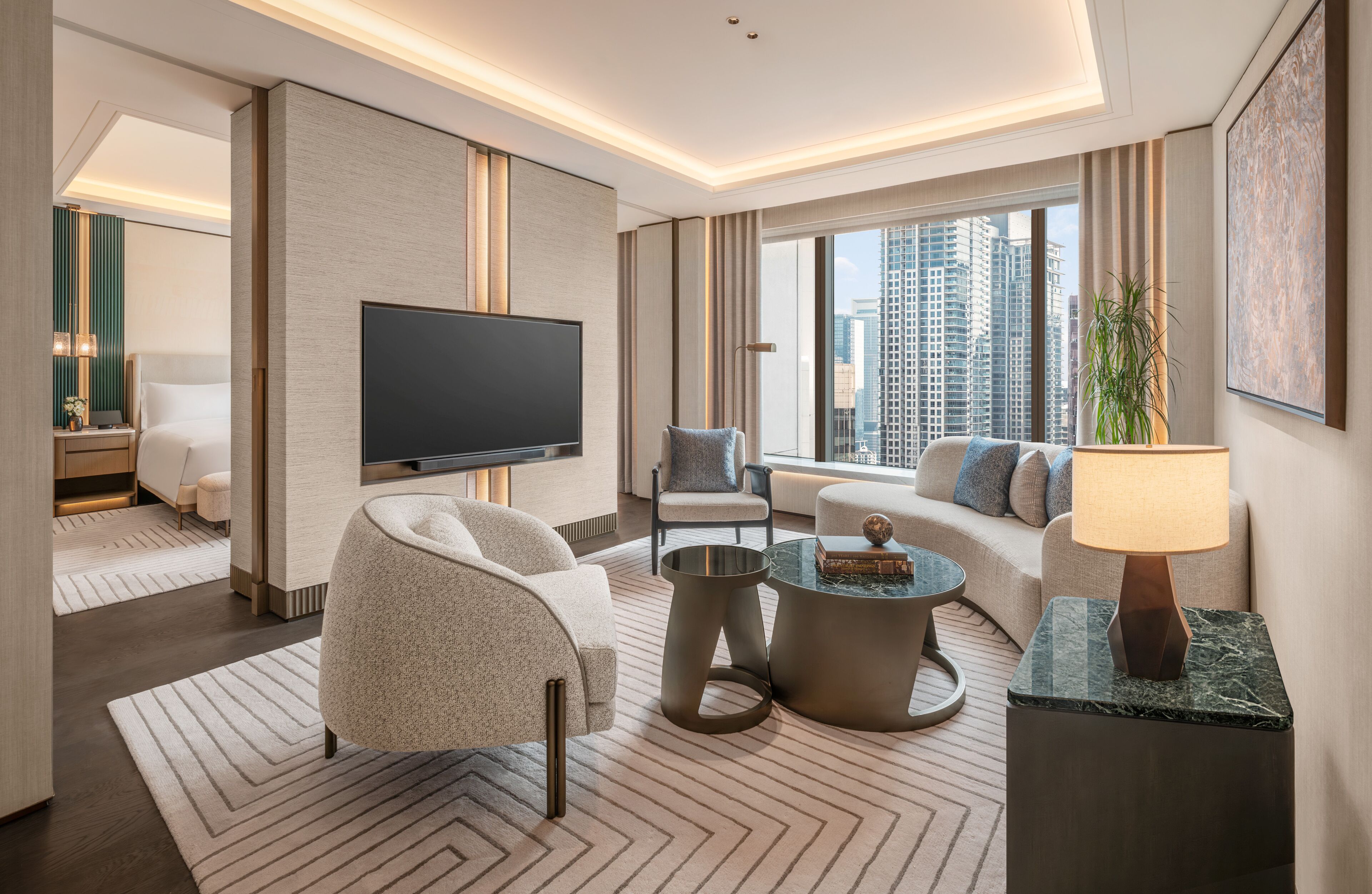 Quarto de hotel moderno com televisão de tela plana, assentos confortáveis, mesa de centro e uma grande janela com vista para a cidade.