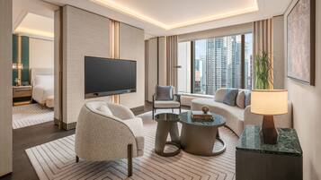 Quarto de hotel moderno com televisão de tela plana, assentos confortáveis, mesa de centro e uma grande janela com vista para a cidade.