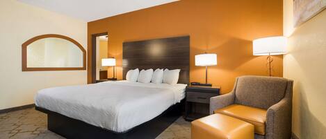 Quarto de hotel com uma cama grande, uma cadeira, uma mesinha de cabeceira e uma luminária.