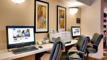 Espaço de trabalho em hotel, com dois computadores de mesa, uma impressora e cadeiras de escritório.