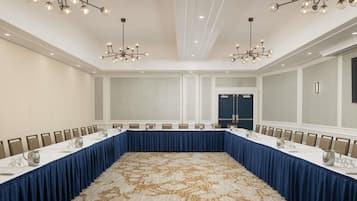 Uma sala de conferências com uma mesa comprida, cadeiras e lustres.