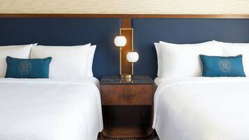 Quarto de hotel com duas camas, uma mesa de cabeceira com abajur e um tapete estampado.