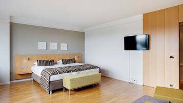 Quarto de hotel moderno com piso de madeira, cama com roupa de cama listrada, televisão de tela plana na parede e um pequeno banco.