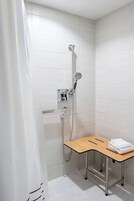 Chuveiro com chuveiro manual, torneira fixa na parede e um banco de madeira com toalhas.
