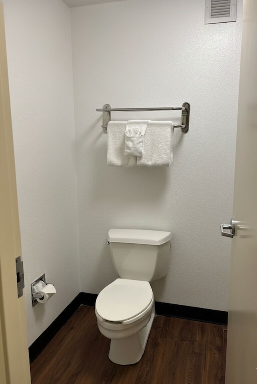 Casa de banho pequena e limpa, com sanita branca, porta-toalhas e suporte para papel higiénico.