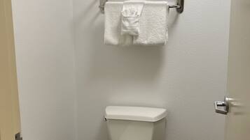 Casa de banho pequena e limpa, com sanita branca, porta-toalhas e suporte para papel higiénico.