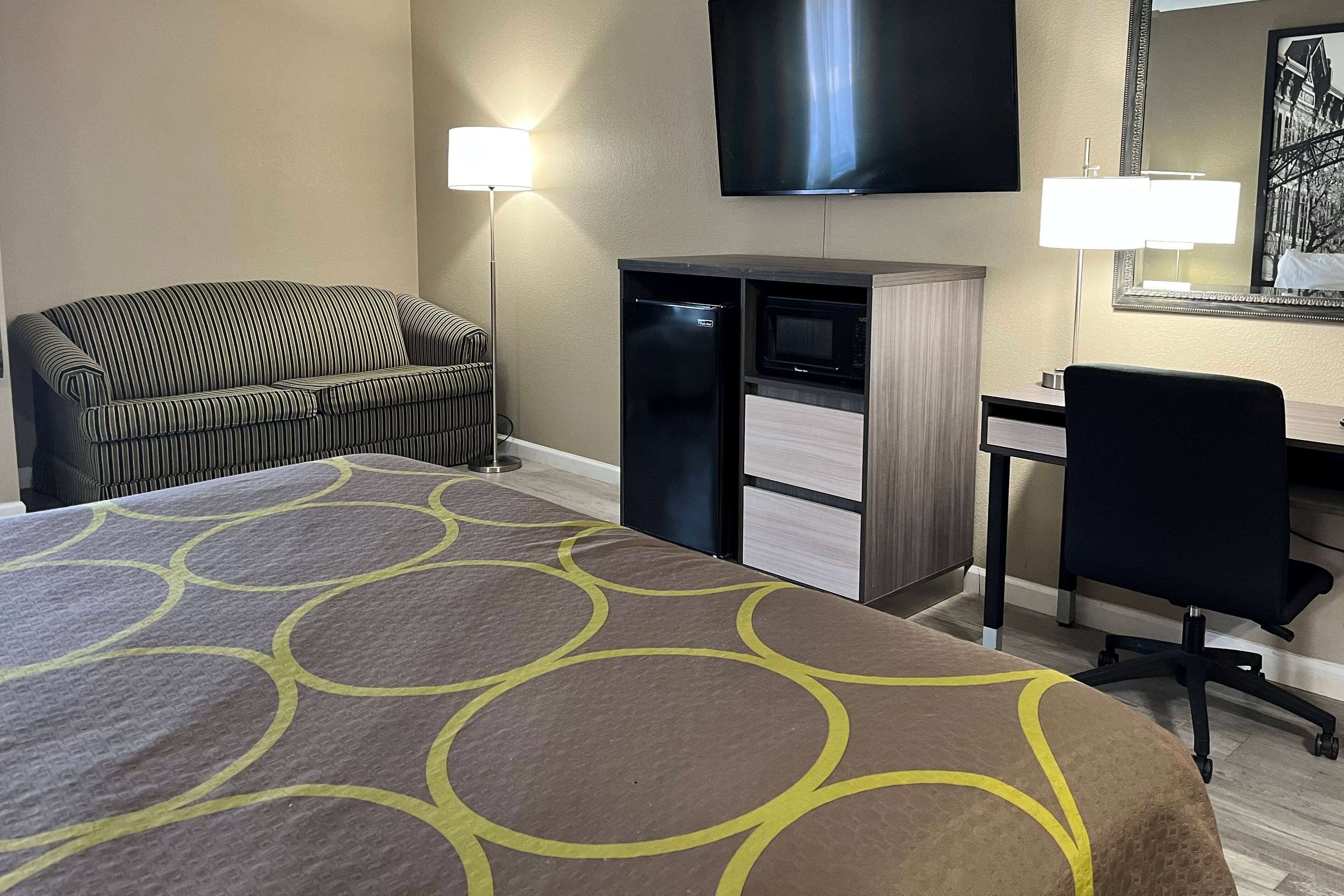 Quarto de hotel com cama, escrivaninha, cadeira, televisão e espelho.
