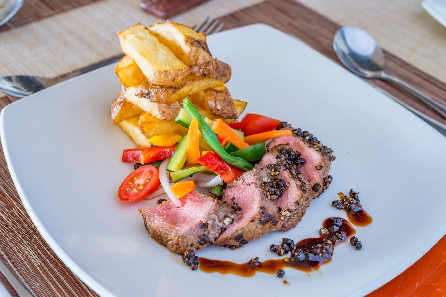 Um prato com bife, legumes e batatas fritas.