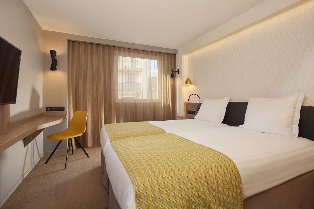 Quarto de hotel com uma cama, uma escrivaninha, uma cadeira e uma televisão.