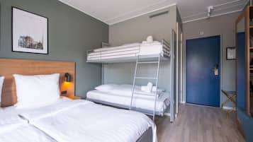 Quarto de hotel com beliche, cama de solteiro, cabeceira de madeira, quadro com vista urbana emoldurada e porta azul.