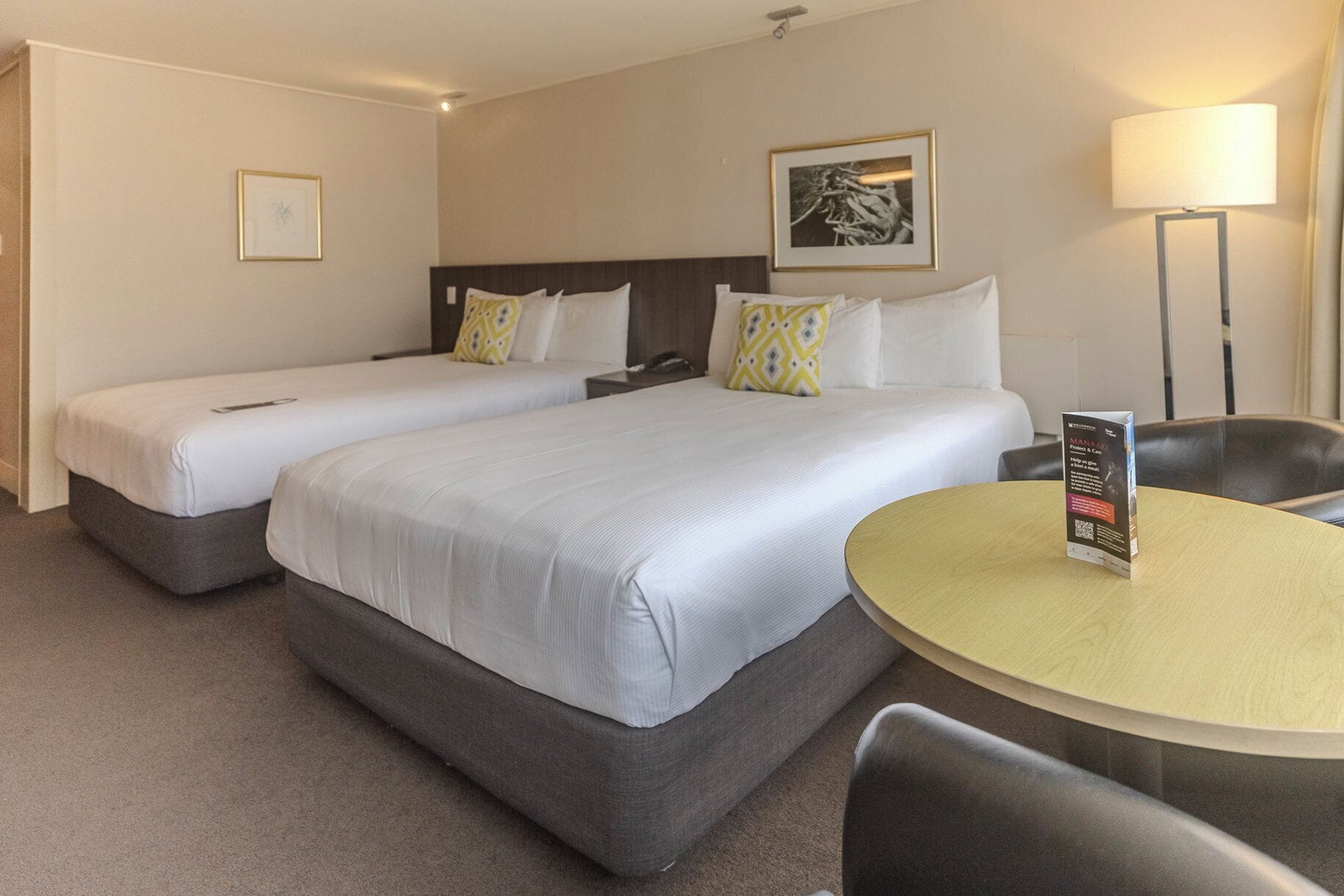 Quarto de hotel com duas camas, uma mesa redonda e uma cadeira.