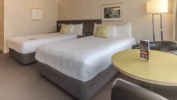 Quarto de hotel com duas camas, uma mesa redonda e uma cadeira.