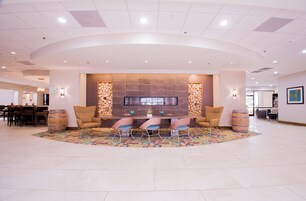 Um hall amplo com área de estar central, destacando uma mesa comprida e cadeiras, parede decorativa com lareira e piso de azulejos.