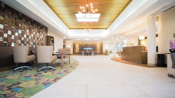 Um saguão de hotel com balcão de recepção, área de estar e uma tela de televisão.