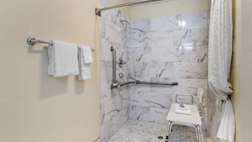 Um banheiro moderno com chuveiro, barras de apoio, um banquinho pequeno e porta-toalhas.