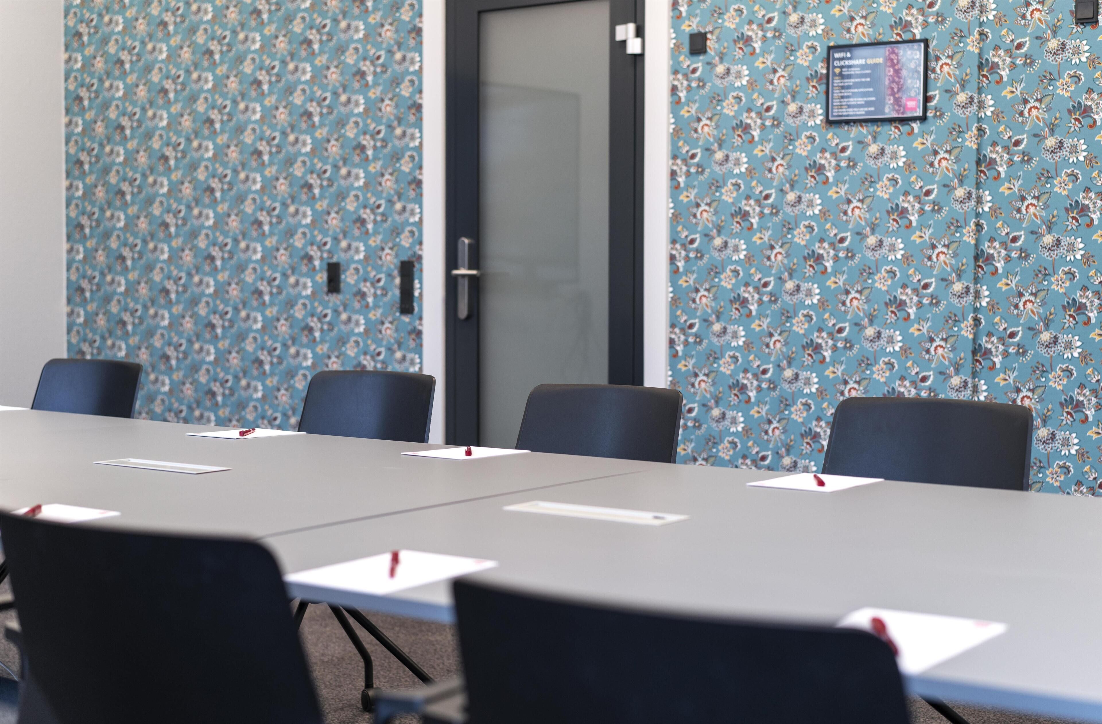 Uma sala de conferências com uma mesa comprida, cadeiras e uma porta.