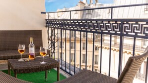 Uma varanda com móveis de vime, duas taças de vinho e uma garrafa de vinho.