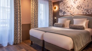 Uma cama de casal com cabeceira cinza, duas almofadas e um cobertor estampado.