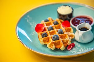 Um prato com waffles, amoras e dois potinhos de xarope e geleia.