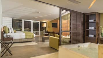Quarto de hotel moderno com uma cama grande, área de estar com sofá e poltronas, banheira e um painel de madeira.