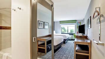 Quarto de hotel moderno com cama, escrivaninha, televisão e chuveiro.