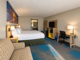 Quarto de hotel com cama, escrivaninha, cadeira, televisão e banheiro.
