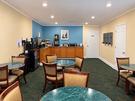 Quarto de hotel com área de refeições, cozinha compacta e porta para um corredor.