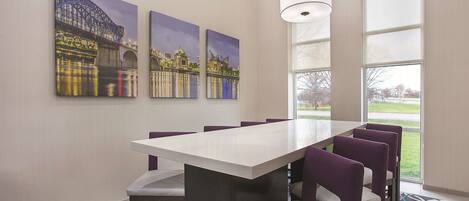 Uma sala de conferências com uma mesa comprida, cadeiras roxas e três quadros com paisagens urbanas na parede.