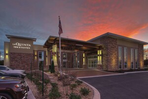 Entrada de hotel com placa indicando "La Quinta Inn & Suites", uma bandeira americana e área de estacionamento com carros.