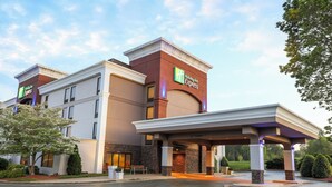 Edifício Holiday Inn Express com entrada coberta, detalhes em pedra e área ajardinada com um banco.