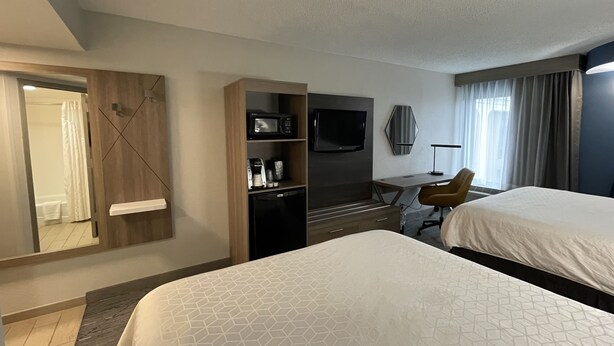 Quarto de hotel com duas camas, uma escrivaninha com cadeira, televisão, micro-ondas e cafeteira.
