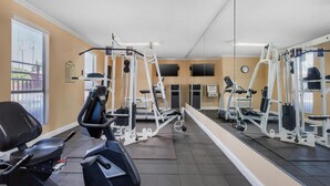 Uma academia com diversos equipamentos de exercício, um espelho na parede e um relógio.