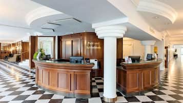 Uma área de recepção de hotel com balcão de check-in, mesa de atendimento e máquina de check-in.