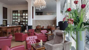 Uma sala de estar ampla com sofás de couro vermelho, um bar e um lustre.