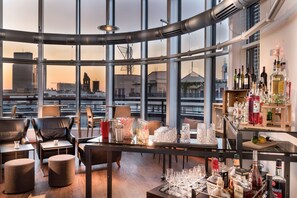 Uma área de bar moderna com vista panorâmica da cidade, assentos de couro e uma variedade de garrafas e copos.