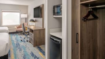 Quarto de hotel com cama, escrivaninha, cadeira, luminária, televisão, micro-ondas e guarda-roupa de madeira.