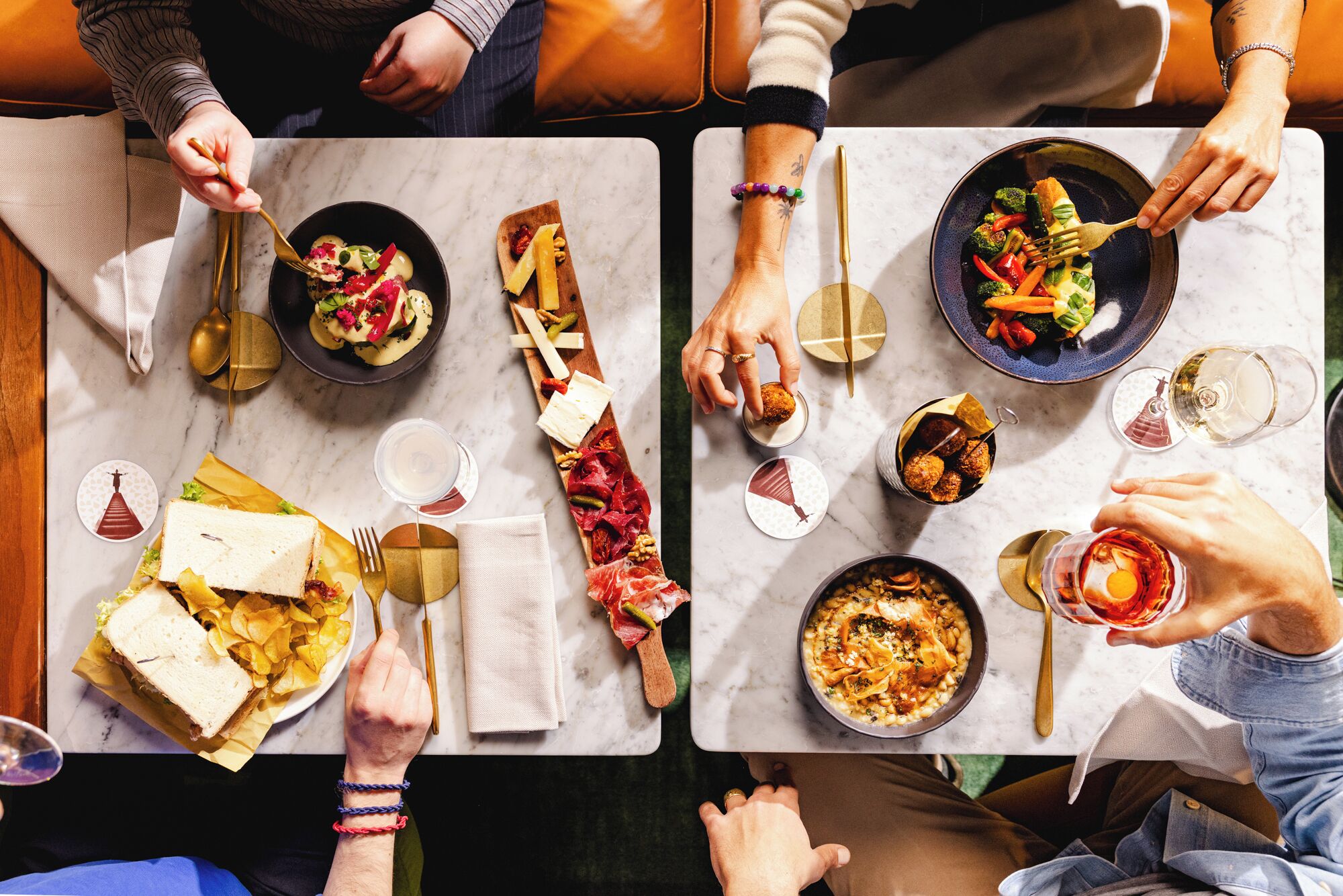 Um grupo de pessoas jantando à mesa, com diversos pratos, incluindo um sanduíche, salada e uma tábua de queijos.