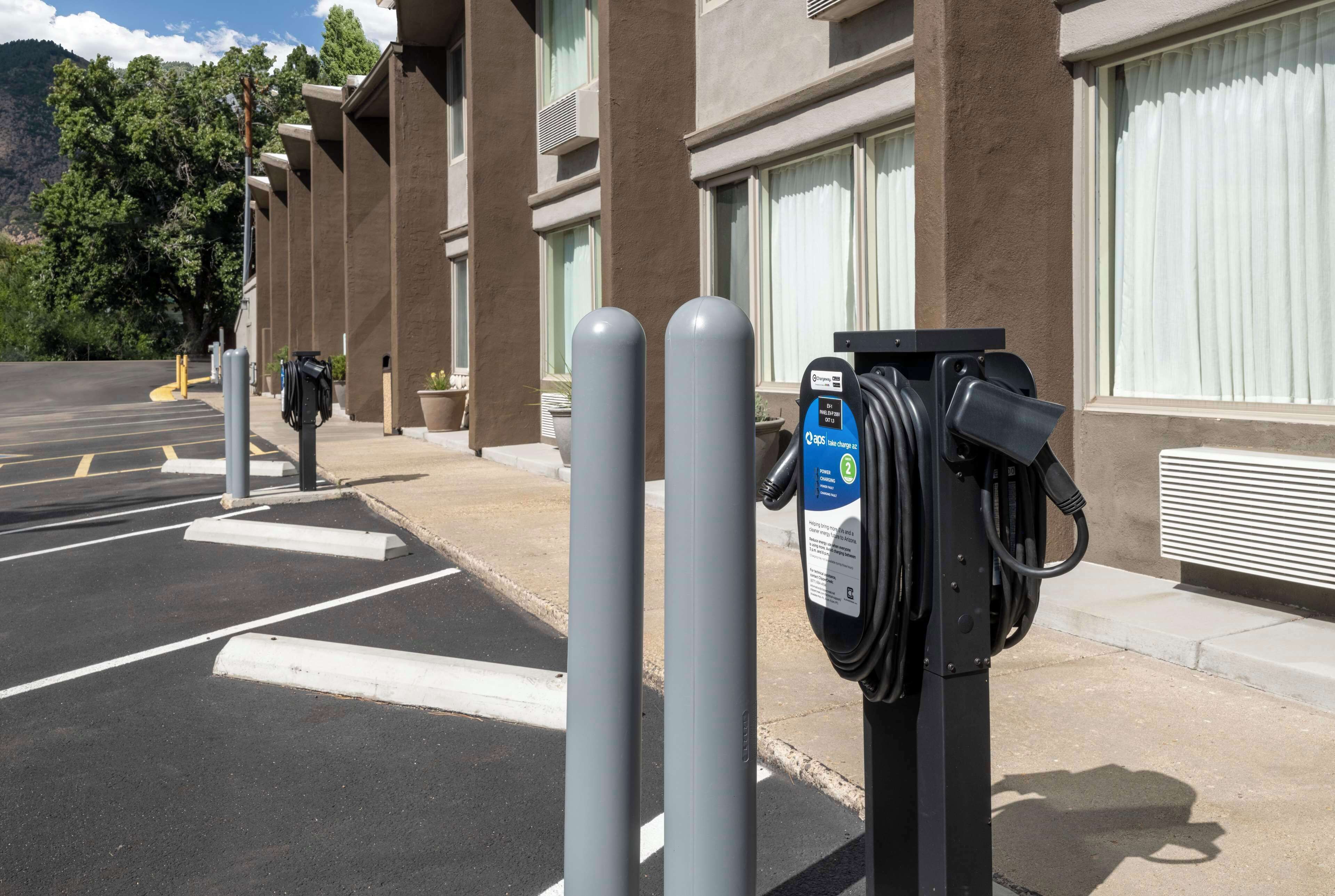 Uma área de estacionamento com estações de carregamento para veículos elétricos, um edifício com grandes janelas e céu claro.