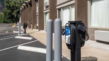 Uma área de estacionamento com estações de carregamento para veículos elétricos, um edifício com grandes janelas e céu claro.