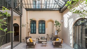Um espaço amplo e interno com piso estampado, dois sofás com almofadas, uma mesa pequena e uma bicicleta.